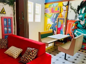 Um quarto com um sofá vermelho, uma mesa pequena e um mural colorido na parede.
