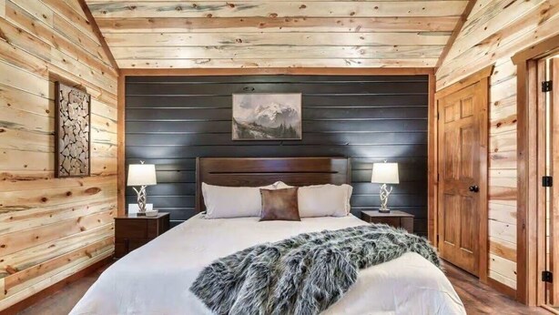 Quarto com painéis de madeira, uma cama, duas mesas de cabeceira e um quadro pendurado.