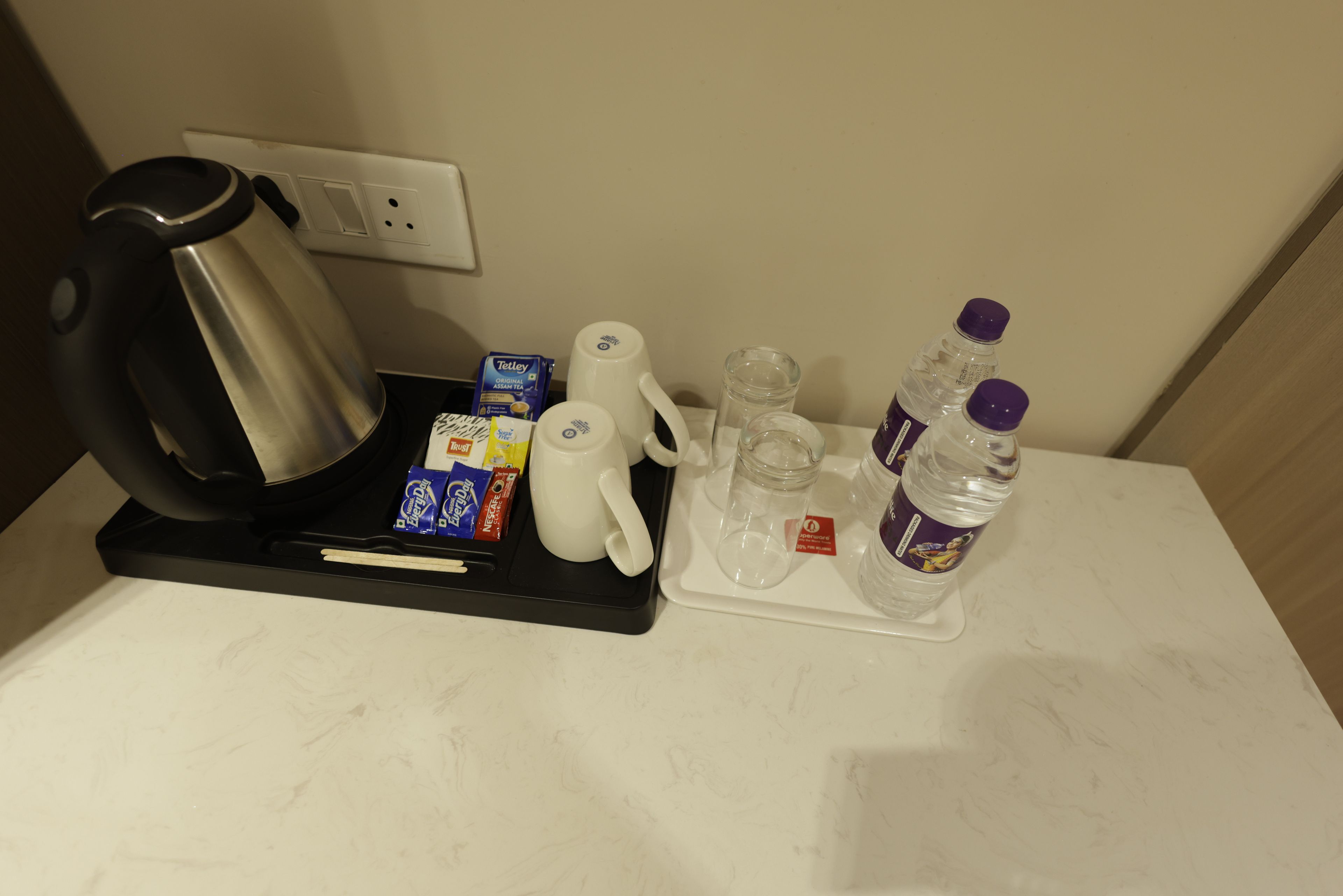 Bandeja de café da manhã em quarto de hotel, com cafeteira, sachês de chá, sachês de açúcar, caneca e água engarrafada.