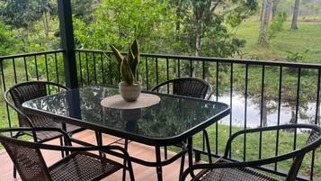 Mesa com tampo de vidro, quatro cadeiras, um vaso com planta e vista para a paisagem natural.