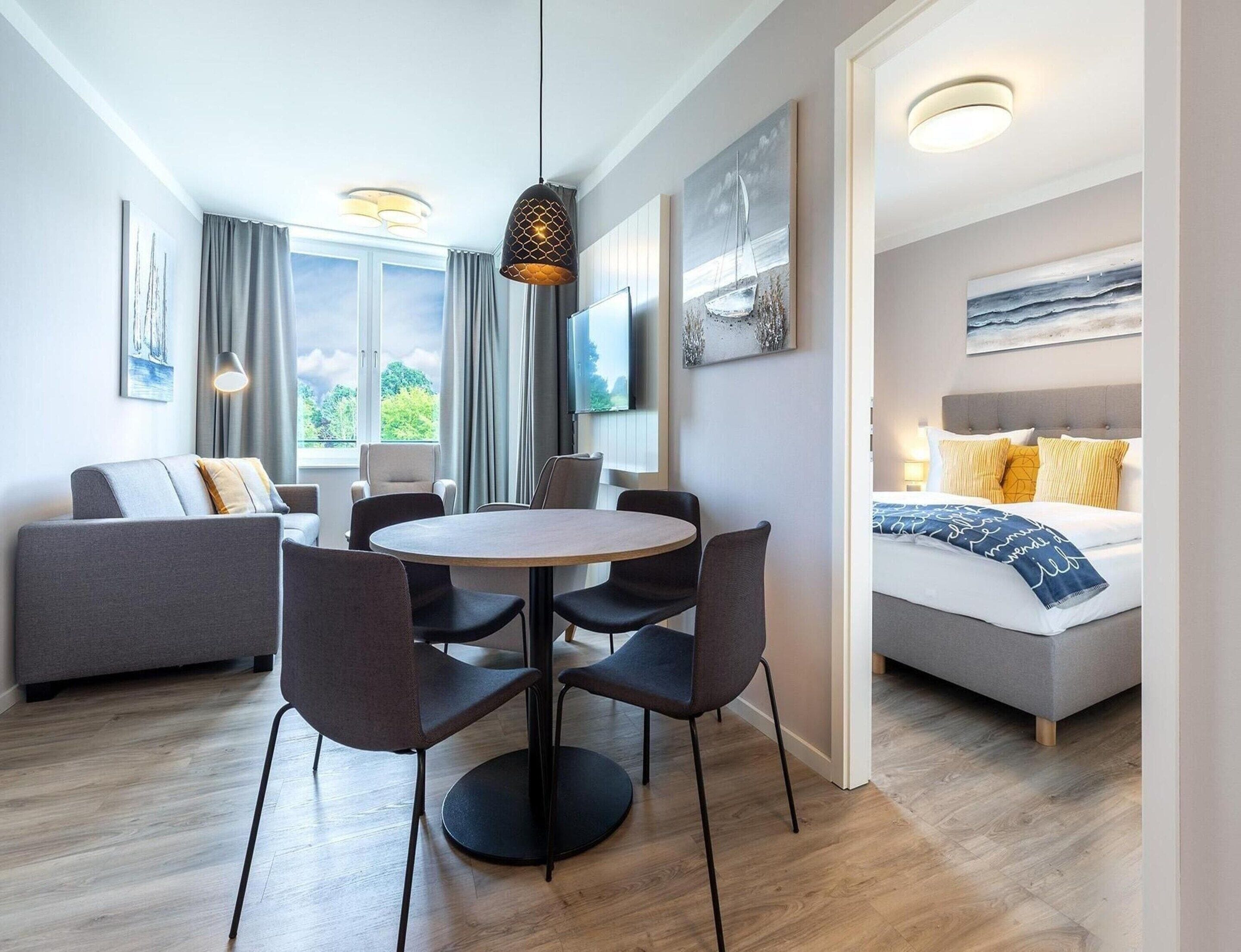 Quarto de hotel moderno com área de refeições, sofá, cama e obras de arte nas paredes.