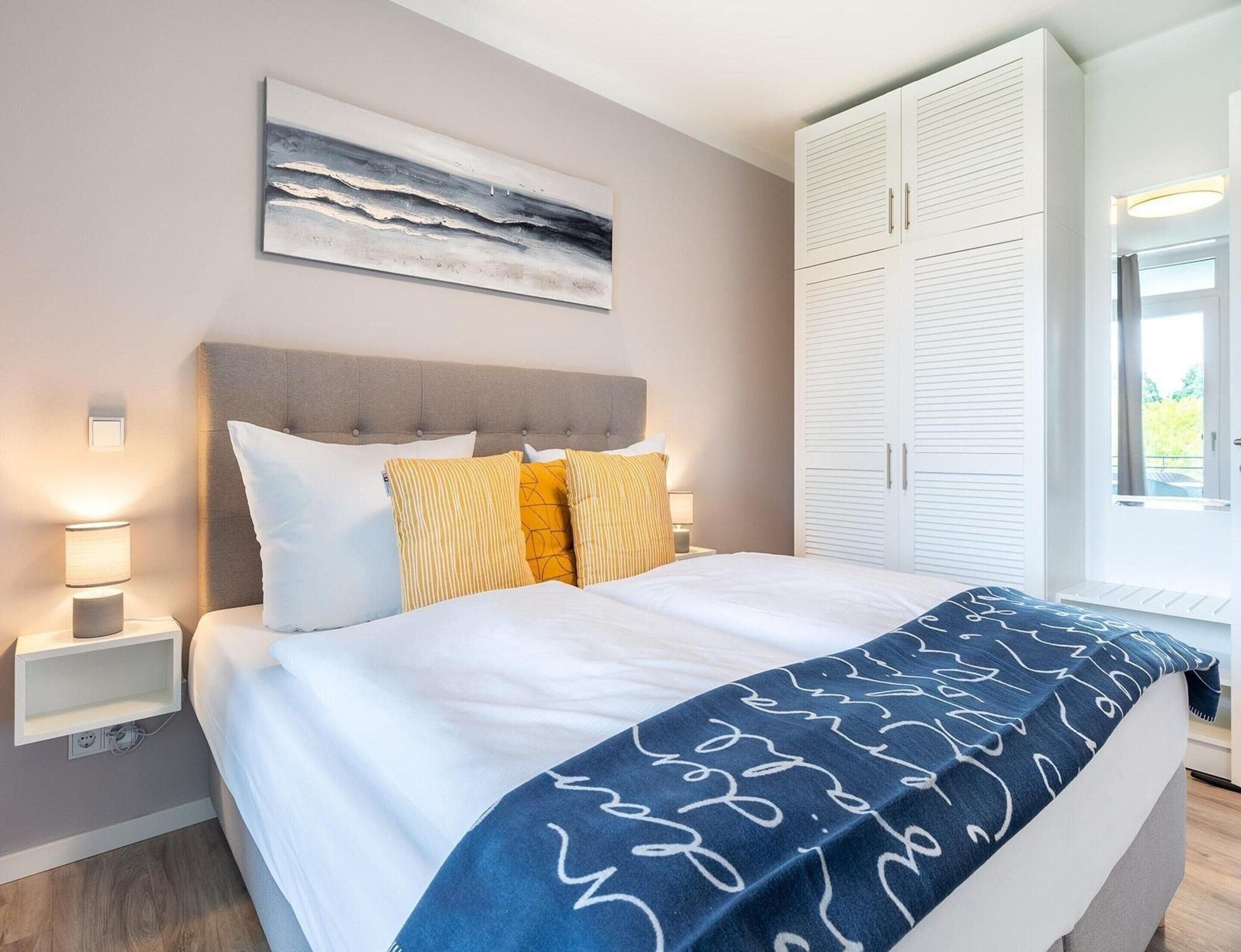 Quarto com cama, luminárias de cabeceira, painel de cabeceira, guarda-roupa e um quadro na parede.