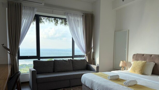 Quarto de hotel com uma janela grande, um sofá, uma cama com cabeceira e um tapete estampado.