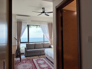 Quarto com sofá, ventilador de teto, vista para o mar e tapete estampado.
