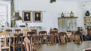 Uma área de refeições com cadeiras de madeira e uma mesa, uma parede de pedra e um armário de madeira com copos.