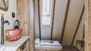 Um quarto pequeno e rústico com uma cama beliche de madeira, uma bacia vermelha com bolinhas e uma janela.