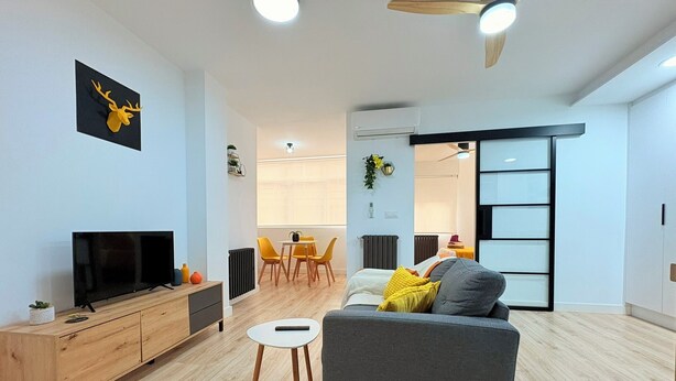Uma sala de estar moderna com sofá, TV e um espaço de jantar com cadeiras.