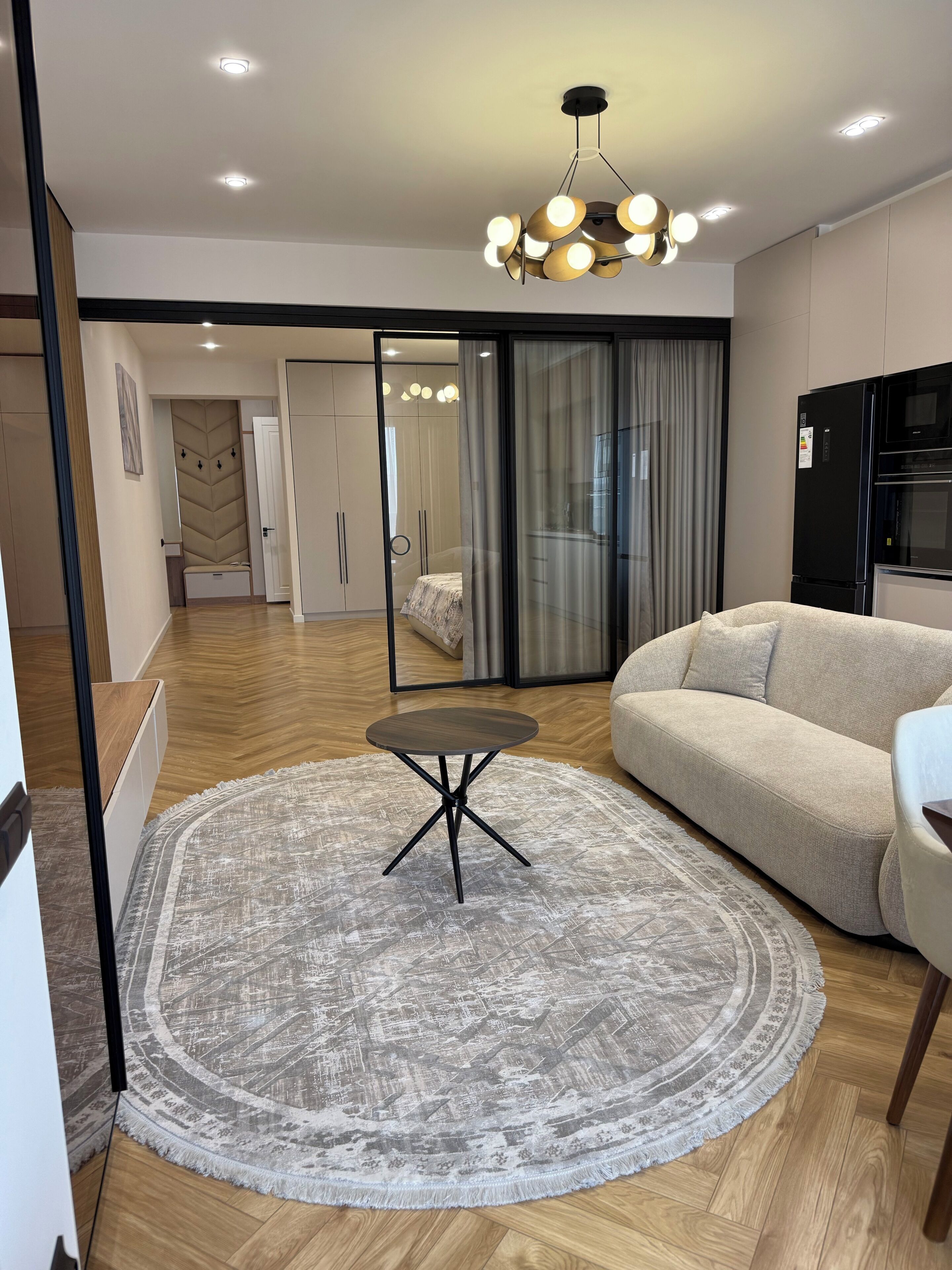 Uma sala de estar moderna com tapete redondo, sofá, mesinha e luminária de teto.