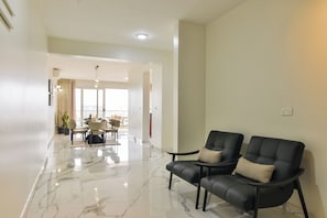 Ampla sala de estar com piso de mármore, área de jantar com mesa e cadeiras, e espaço de estar com duas cadeiras pretas.