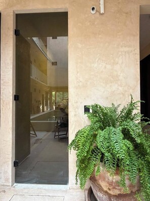 Entrada com planta em vaso, uma porta e vislumbre de um espaço interior com mesa e cadeiras.