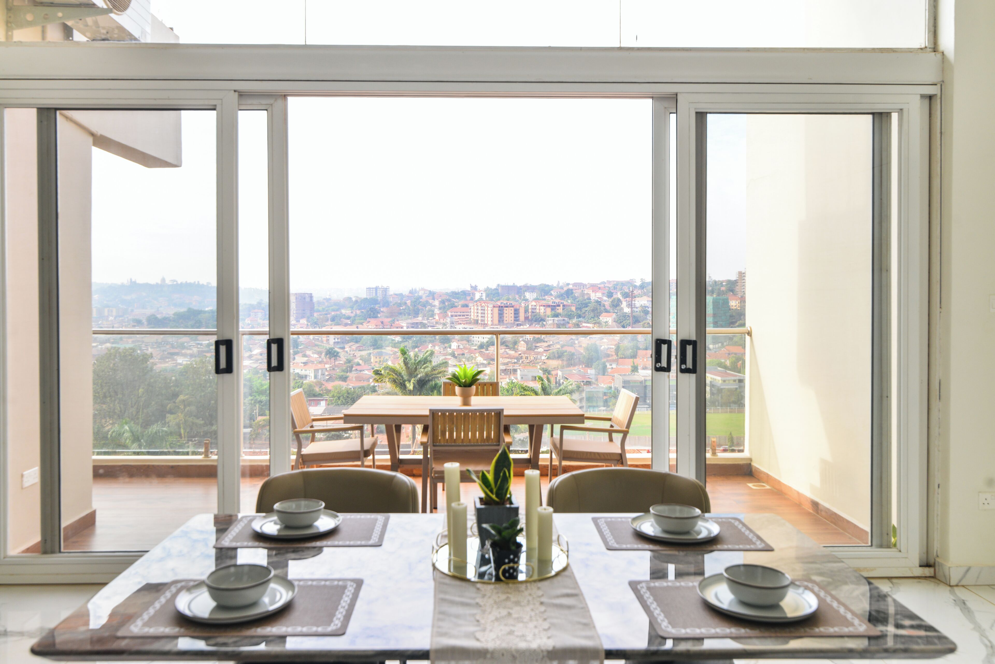 Uma área de jantar com uma mesa posta para quatro, com vista para a cidade através de grandes janelas.