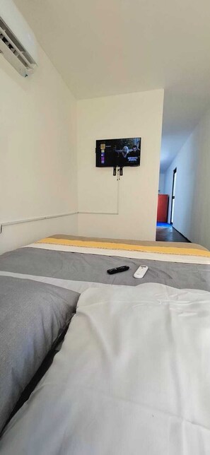 Quarto com uma cama, televisão na parede e controle remoto sobre a cama.