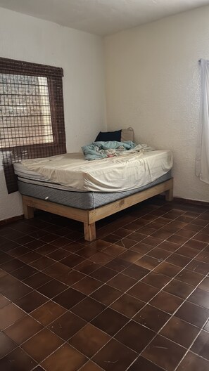 Um quarto com uma cama, uma janela com mosquiteiro e uma cortina.