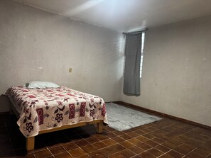 Um quarto com cama, janela com cortina e piso de azulejos.