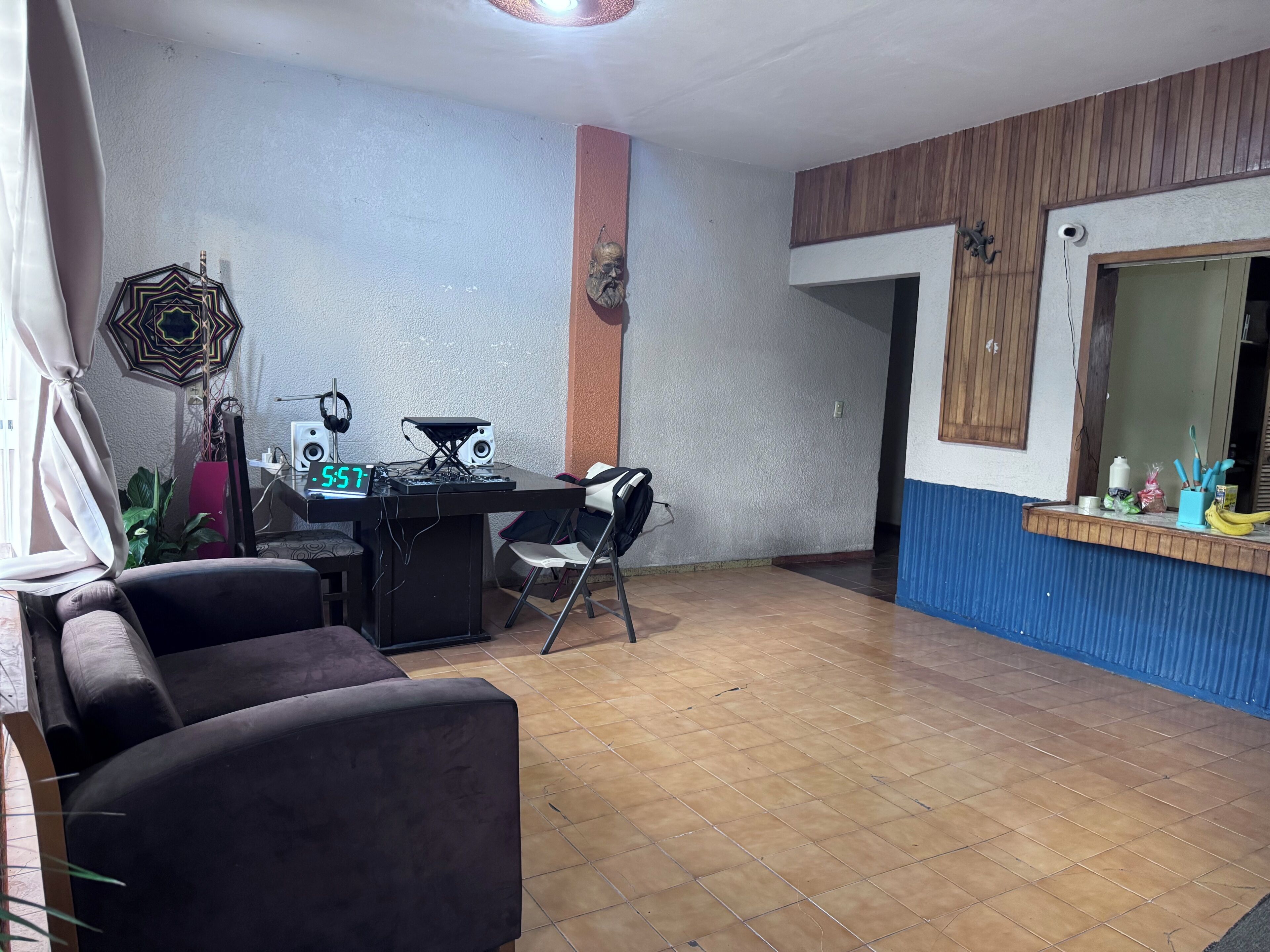 Um quarto com equipamento de DJ, um relógio, uma planta e uma janela com cortinas.