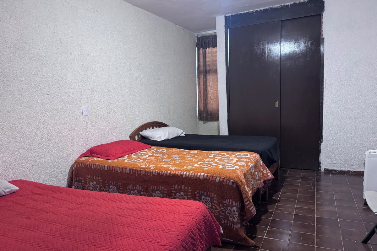 Acomodação pequena, com um quarto só, duas camas, um guarda-roupa e piso ladrilhado.