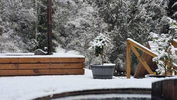 Área externa coberta de neve, com um deck de madeira, estrutura metálica e um pequeno lago.