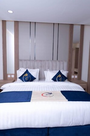 Quarto de hotel com uma cama grande, duas almofadas com logotipo, cabeceira e mesa de cabeceira.