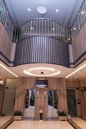Um saguão de hotel moderno com elevador central, corrimão curvo e teto com iluminação embutida.