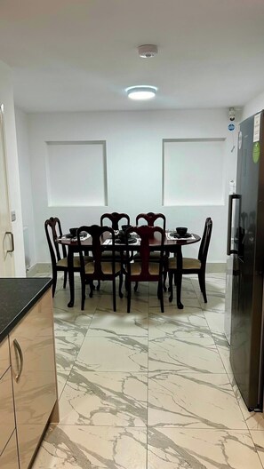 Uma sala de jantar com uma mesa posta para quatro pessoas, rodeada por cadeiras, uma geladeira e um micro-ondas.