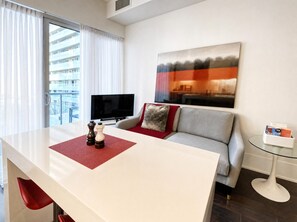 Quarto de hotel moderno com área de refeições, sofá, televisão e um quadro na parede.
