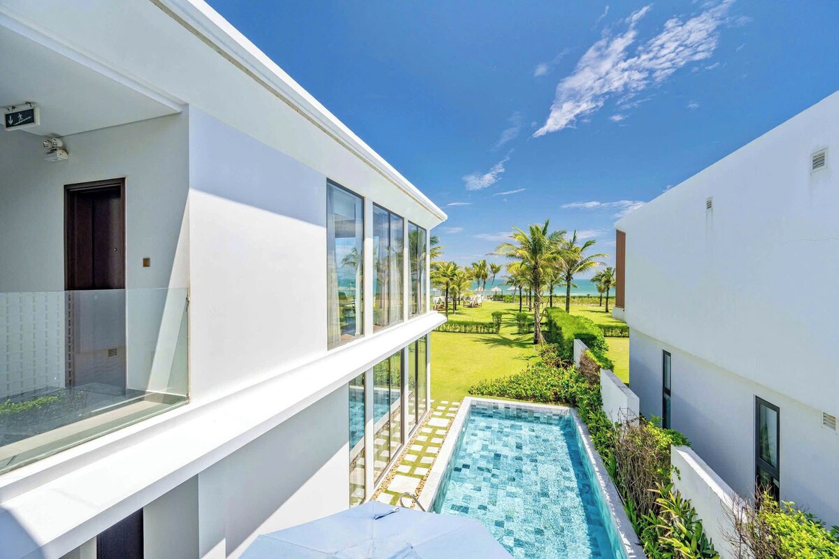 Hotel moderno com piscina, vista clara do oceano e gramado bem cuidado.
