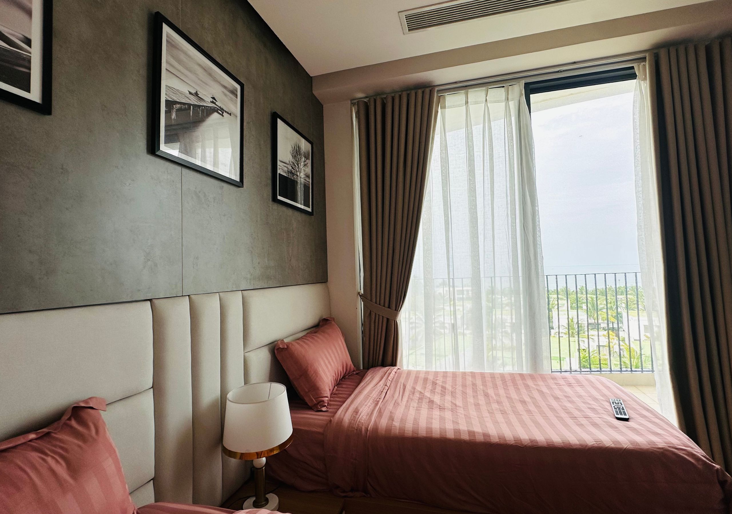 Quarto de hotel com cama, mesa de cabeceira, luminária e duas imagens emolduradas na parede.