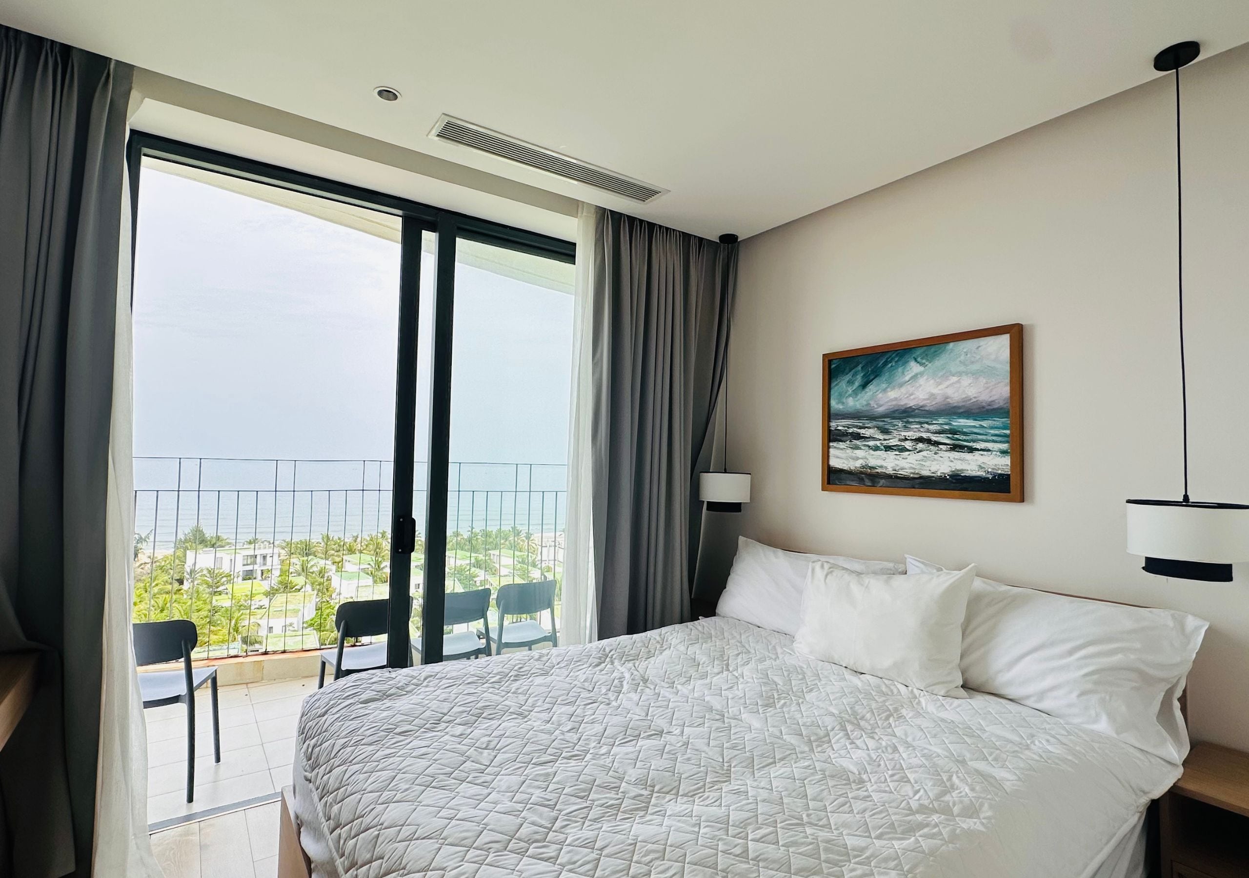 Quarto de hotel com uma cama grande, vista para o mar e varanda com cadeiras.