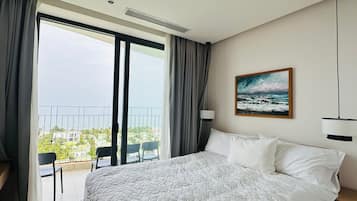 Quarto de hotel com uma cama grande, vista para o mar e varanda com cadeiras.