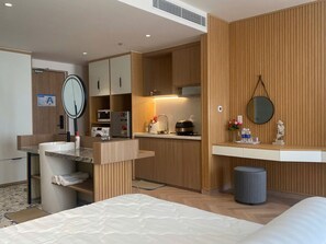 Quarto de hotel compacto com cama, pequeno espaço de cozinha, banheiro com espelho e parede de destaque em madeira.