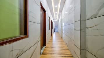 Um corredor com paredes de mármore e soalho de madeira, que leva a uma porta no final.