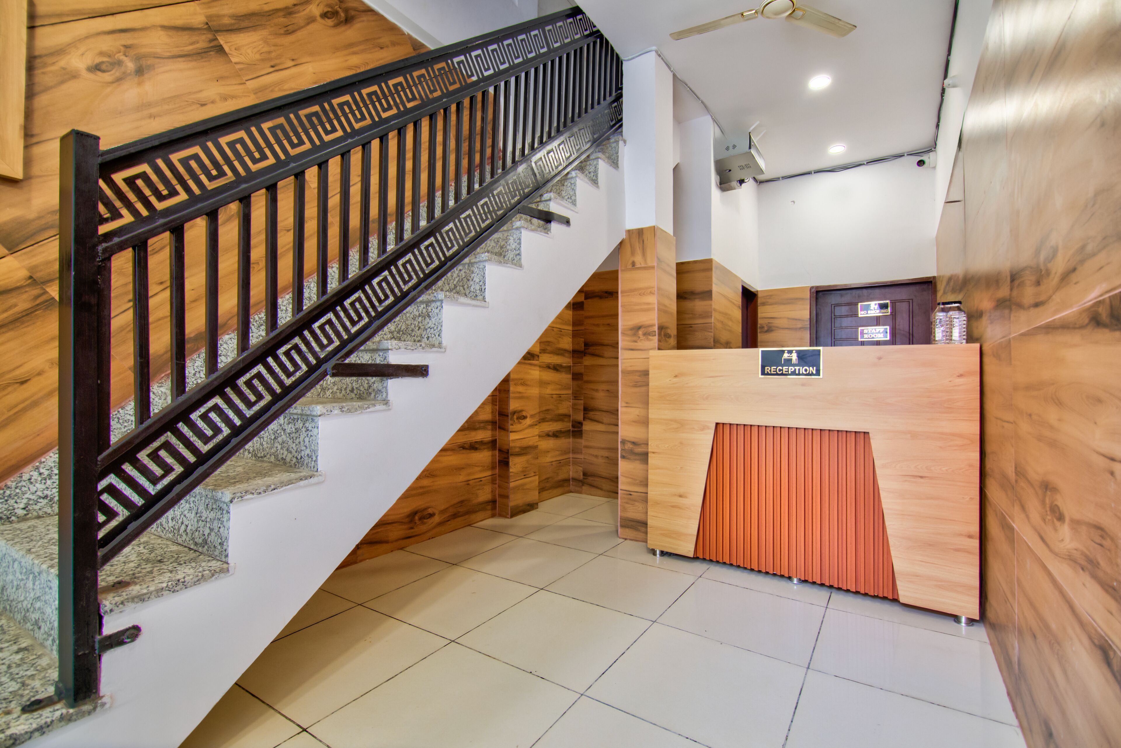 Um balcão de recepção com uma placa, uma escada com guarda-corpo geométrico e lambris de madeira nas paredes.