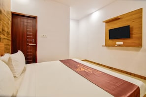 Quarto de hotel com uma cama, uma porta de madeira, uma televisão montada e uma prateleira fixada na parede.