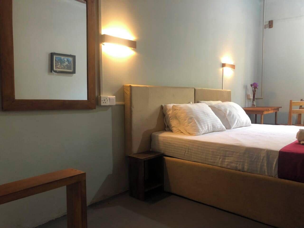 Quarto de hotel com cama, mesa de cabeceira e luminárias fixadas na parede.