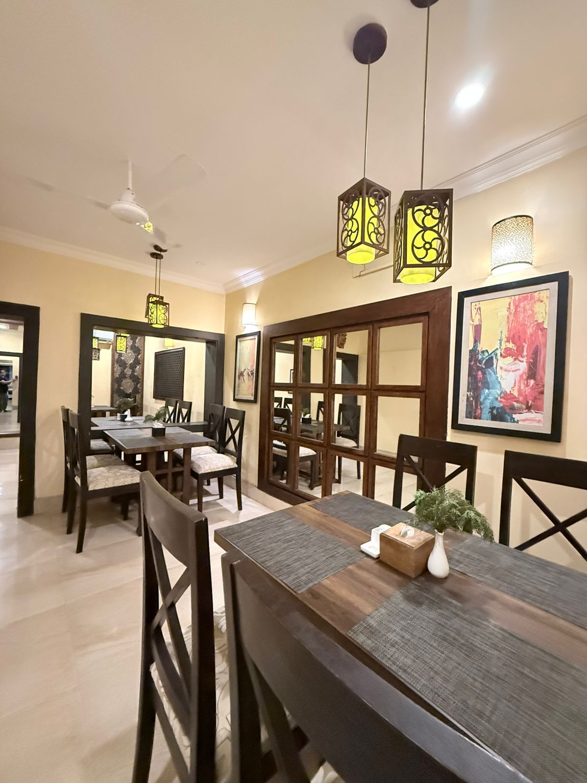 Uma sala de jantar com mesa de madeira, cadeiras, luminárias pendentes e quadros nas paredes.
