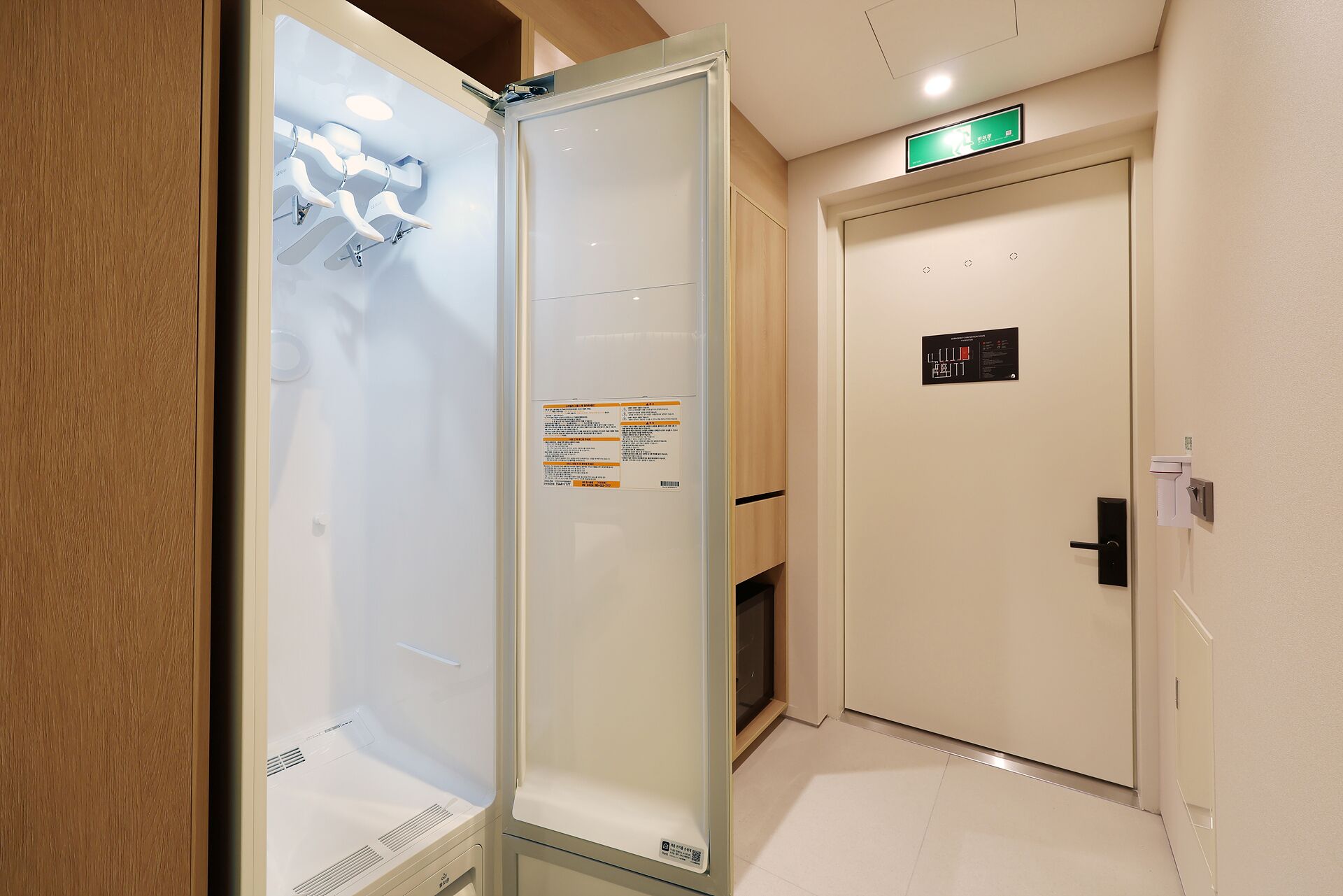 Quarto de hotel com box de vidro, porta com painel de controle e interruptor de luz.