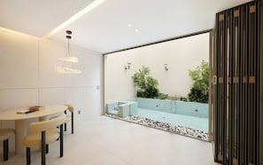 Casa de banho moderna com chuveiro em cabine de vidro, mesa redonda com cadeiras e design minimalista.