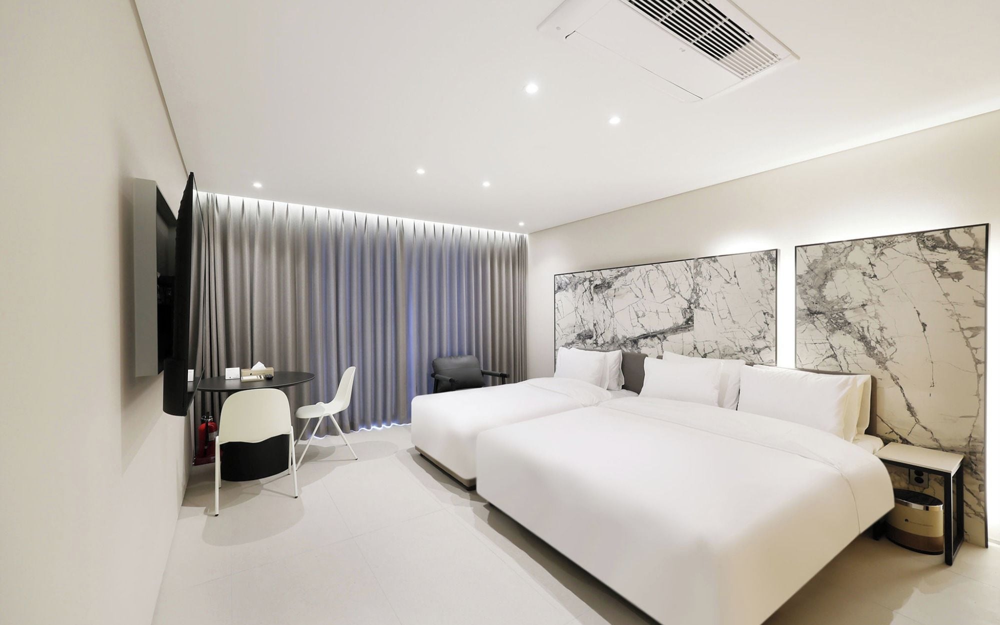 Quarto de hotel moderno com uma cama grande, uma escrivaninha com cadeira, televisão de tela plana e uma janela ampla com cortinas.