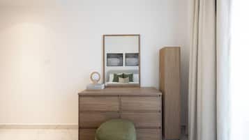 Quarto minimalista com cômoda de madeira, um espelho e um banquinho verde.