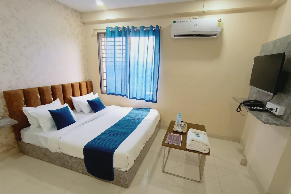 Quarto de hotel com cama, televisão, ar condicionado e janela com cortinas.