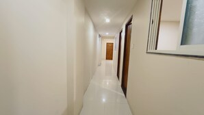 Um corredor com uma porta de madeira no final, paredes brancas e chão de azulejos.