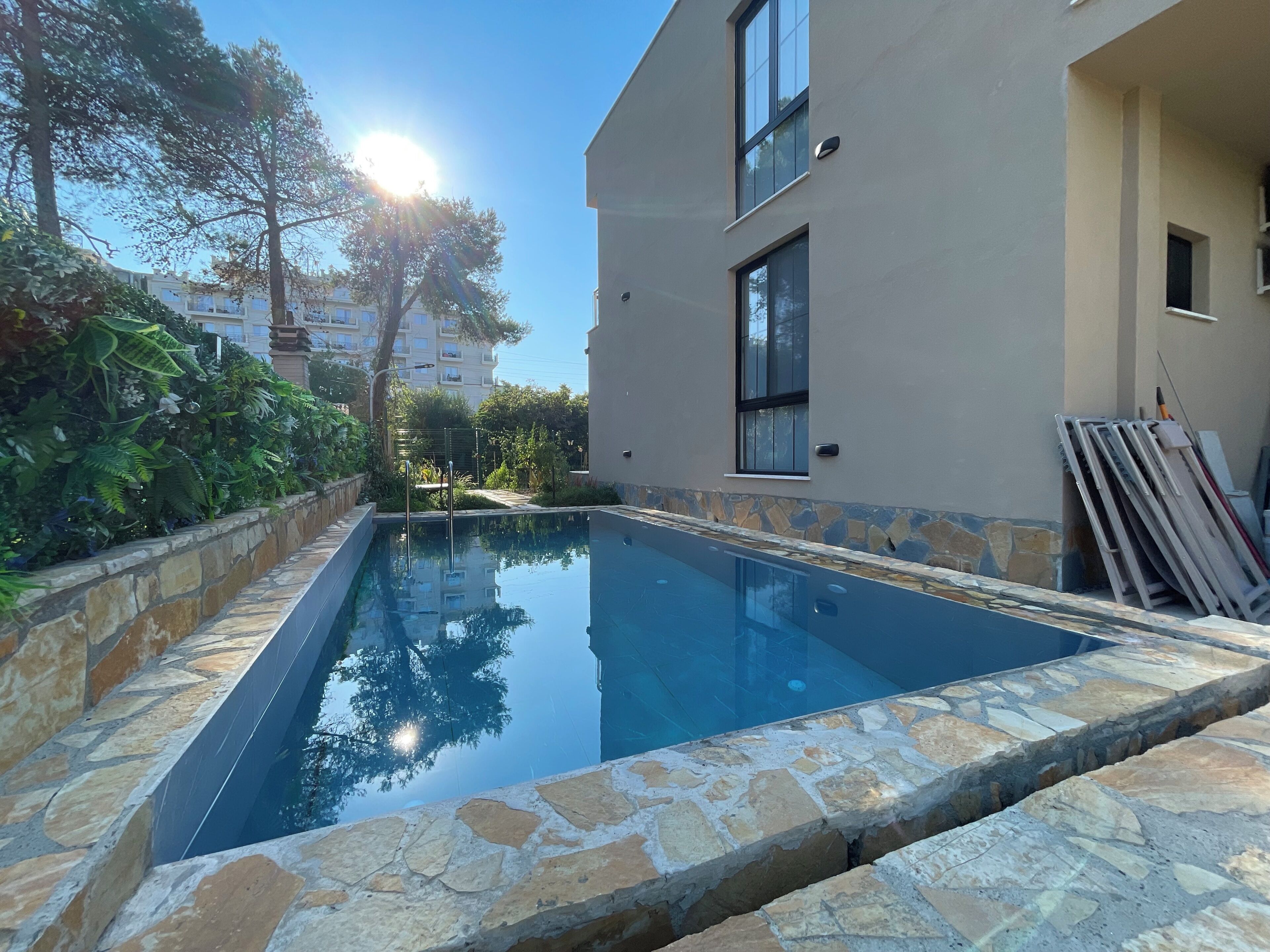 Piscina com borda de pedra, cercada por um muro de pedra e vegetação.