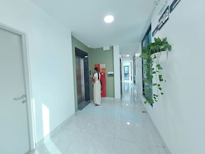 Um corredor com piso de azulejos, um elevador vermelho e uma placa fixada na parede.