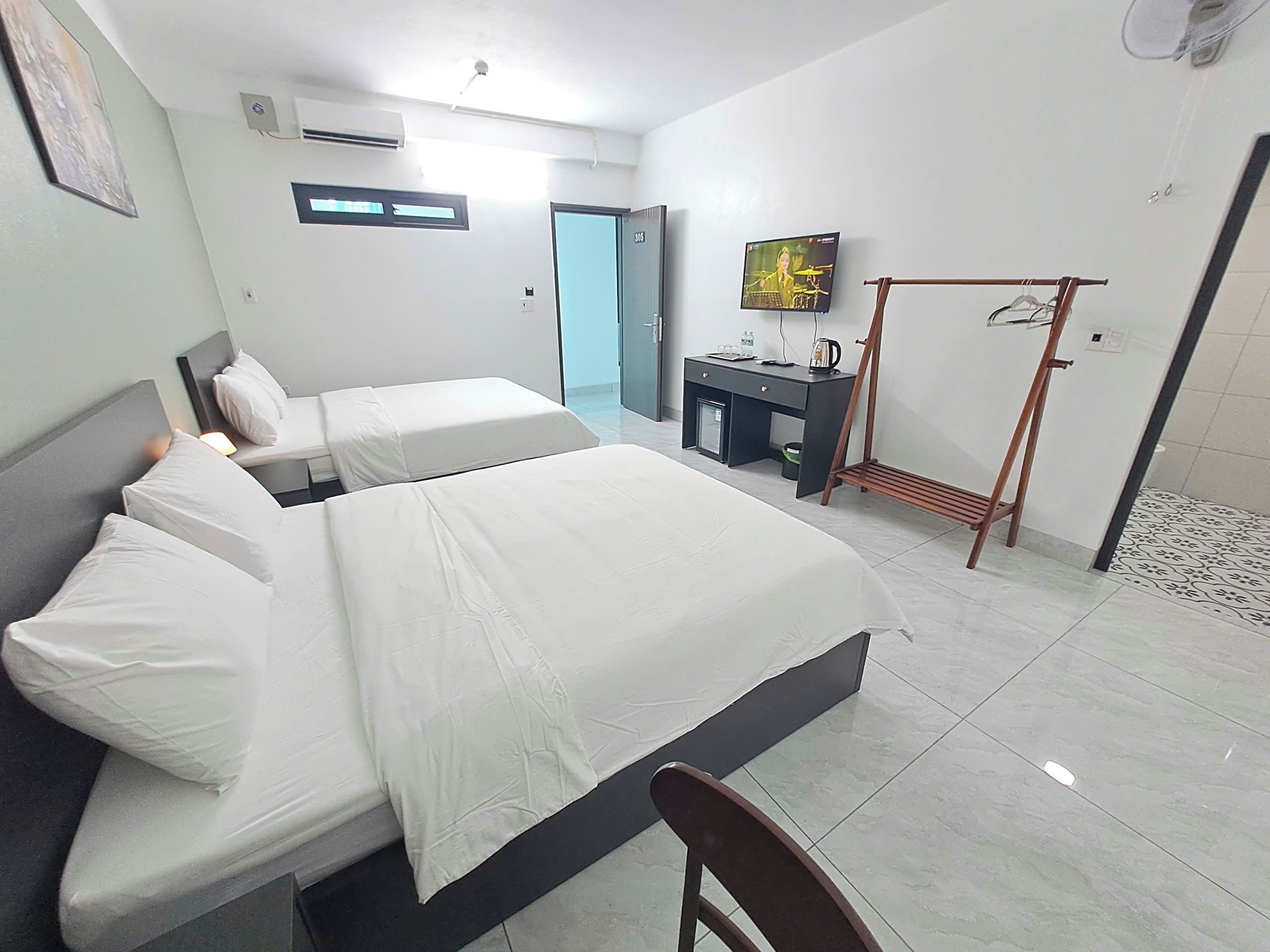 Quarto de hotel com duas camas, uma escrivaninha, uma cadeira, uma televisão e um porta-roupas.
