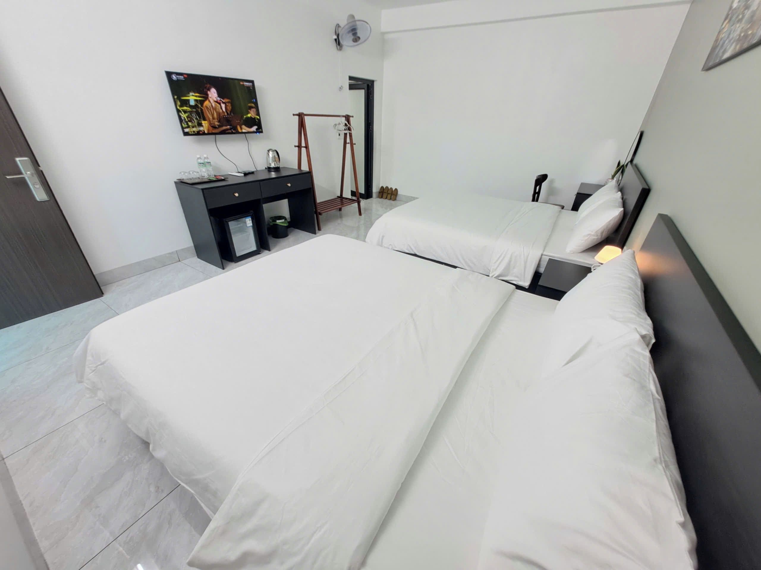 Quarto de hotel com duas camas, uma escrivaninha com televisão e uma kitchenette pequena.