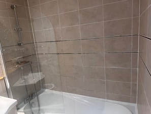 Uma casa de banho moderna com chuveiro de vidro, banheira e paredes revestidas a mosaico bege.