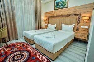 Quarto de hotel com duas camas, uma cabeceira de madeira, um tapete estampado e um quadro na parede.