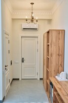 Um corredor com porta branca, um candelabro, um aparelho de ar condicionado e um armário de madeira com uma cafeteira.
