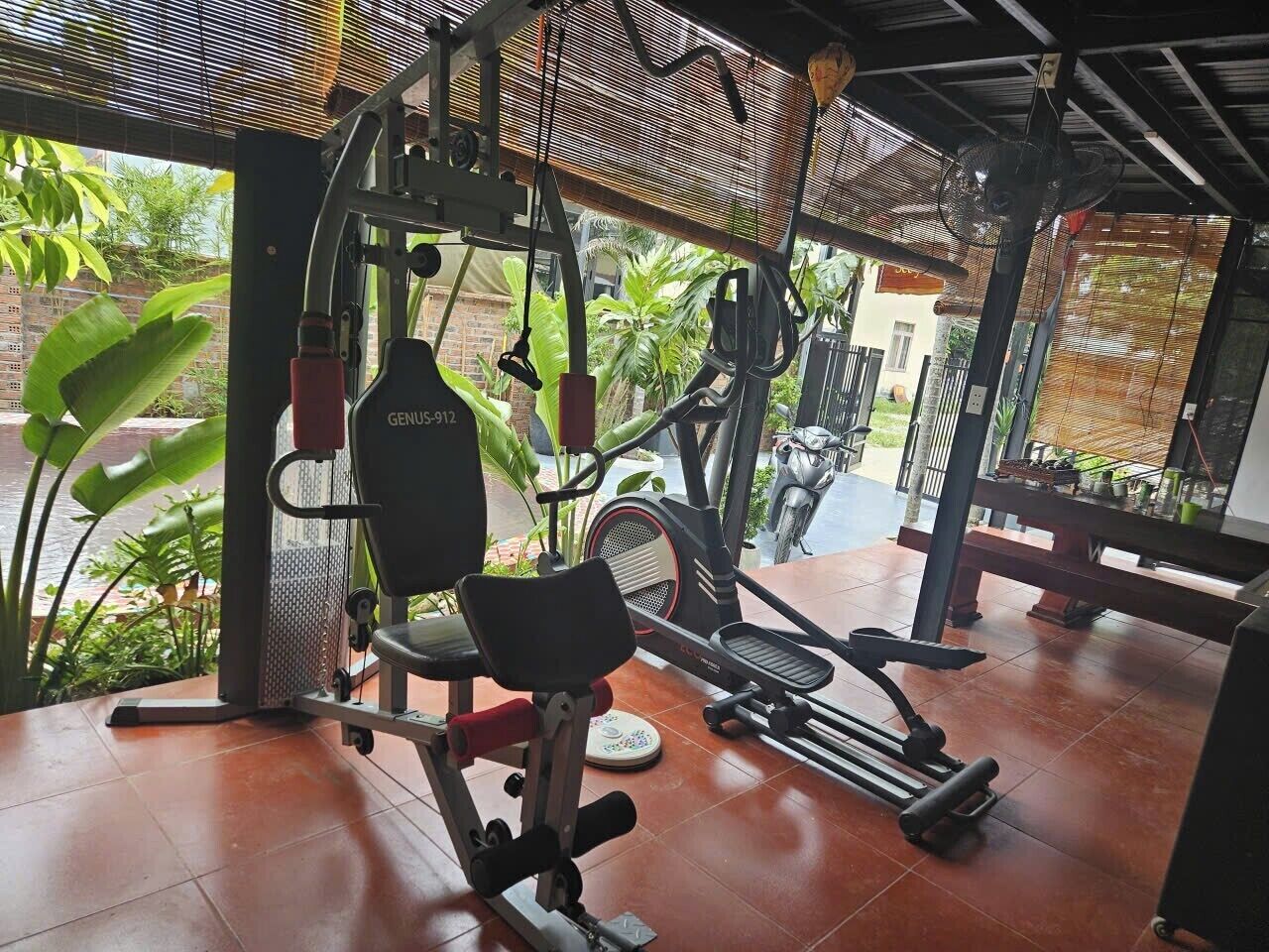 Uma academia com equipamentos de exercício, um ventilador e vista para o exterior.