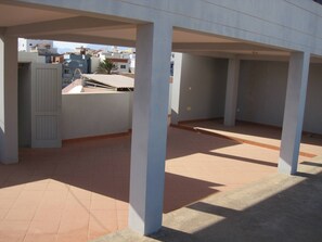 Uma área coberta e vazia, com piso de azulejos e pilares de concreto.